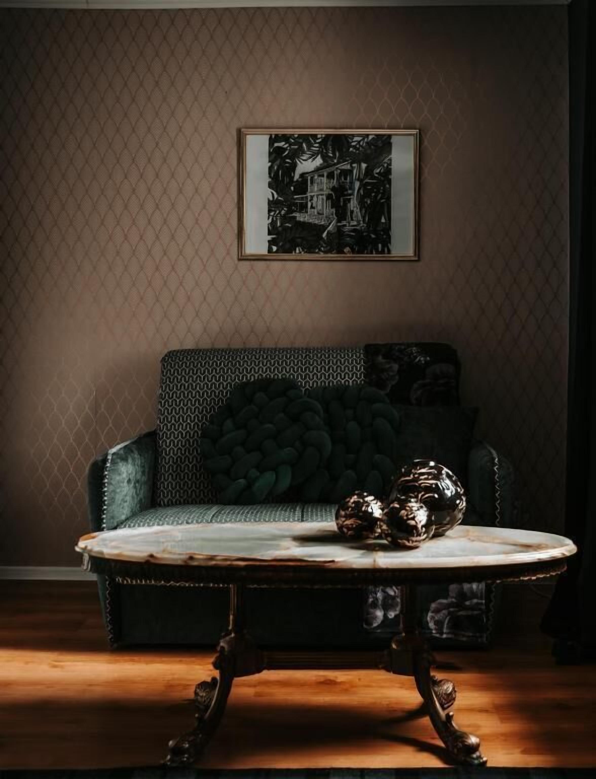 Um quarto com parede estampada, um sofá, uma mesa redonda com objeto decorativo e um quadro na parede.