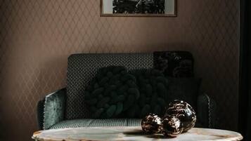 Um quarto com parede estampada, um sofá, uma mesa redonda com objeto decorativo e um quadro na parede.