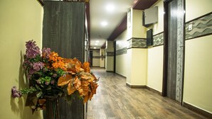 Um corredor com piso de madeira, um vaso com flores fixado na parede e uma porta com design estampado.