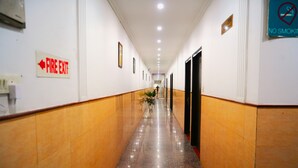 Um corredor de hotel com um sinal de saída de incêndio, um aviso de proibido fumar e uma planta.
