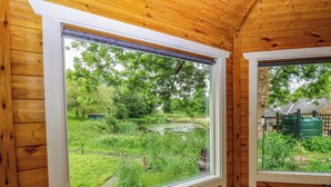 Uma cabana de madeira com uma janela ampla que oferece vista para um lago e vegetação.