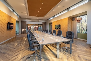Uma sala de conferências com uma mesa comprida, cadeiras e uma televisão na parede.