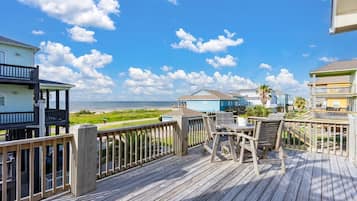 Um deck de madeira com móveis de exterior, com vista para uma praia e o oceano.