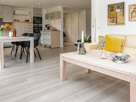 Uma sala de estar moderna com área de jantar, cozinha ao fundo e um sofá com almofada amarela.