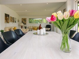 Uma sala de jantar com uma mesa posta para quatro pessoas, um vaso de tulipas e vista para a sala de estar.