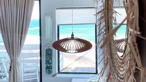 Quarto com uma grande janela com vista para a praia, um tapete de parede tecido, luminária pendente e uma mesa de madeira.