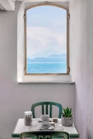 Uma mesa com vista para o mar através de uma janela, uma cadeira verde e um vaso de planta.