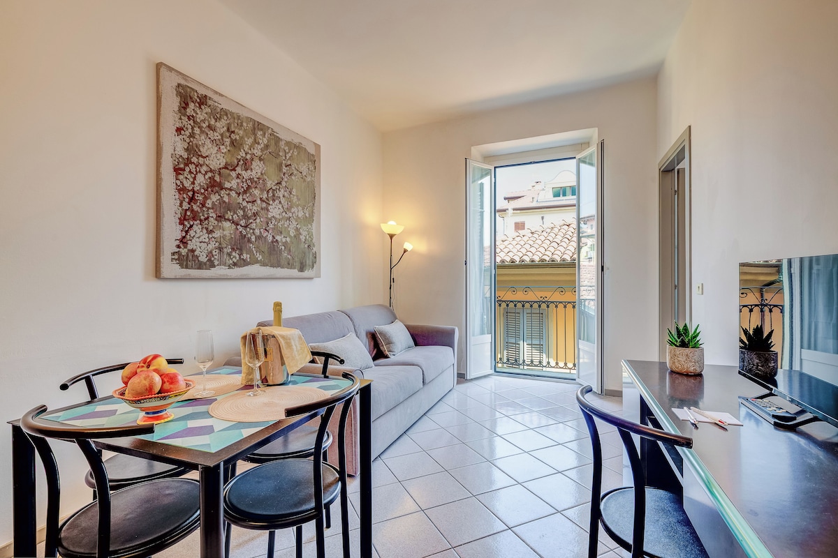 Uma sala de estar moderna com área de jantar, um sofá, uma mesa com uma tigela de frutas e um quadro na parede.
