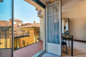 Varanda com vista para edifícios vizinhos, porta de correr em vidro e uma pequena mesa com uma cadeira.