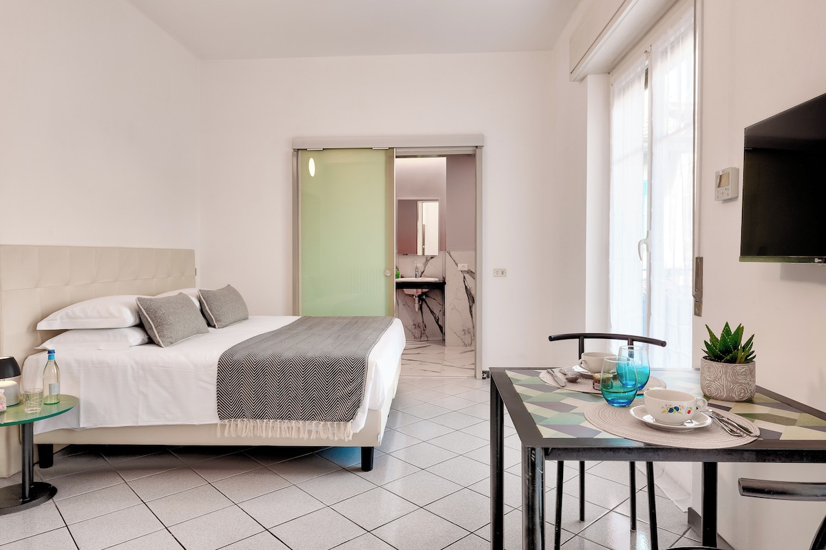 Quarto de hotel com cama, mesa de cabeceira e área de refeições com mesa e cadeiras.