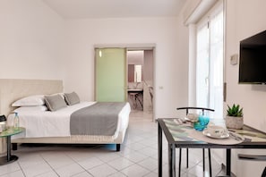 Quarto de hotel com cama, mesa de cabeceira e área de refeições com mesa e cadeiras.