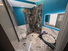 A bathroom with a marble shower, a toilet, and a sink.