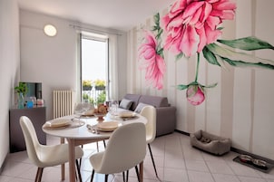 Uma área de refeições com uma mesa posta para quatro pessoas, cadeiras, um sofá e um grande mural floral na parede.
