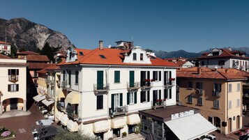 Um edifício com vários andares, varandas, telhado de telhas vermelhas e montanhas ao fundo.