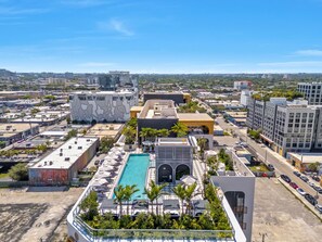 Piscina no terraço com espreguiçadeiras e guarda-sóis, cercada por edifícios e vegetação.