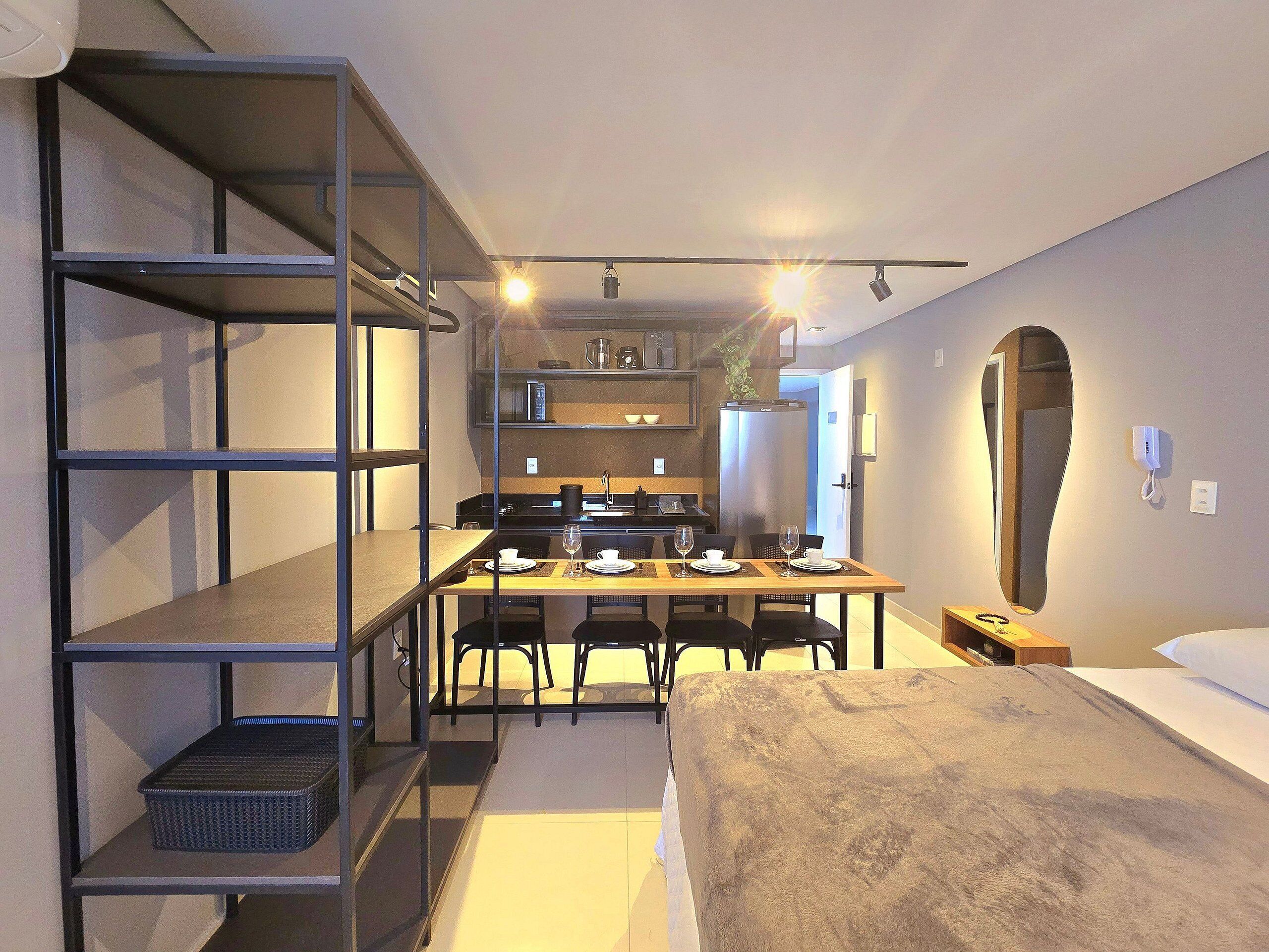 Quarto de hotel compacto com cozinha compacta, área de refeições, cama e um espelho grande.
