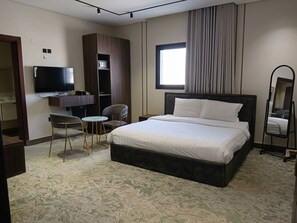 Quarto de hotel com cama, televisão, escrivaninha e cadeira, e janela com cortinas.