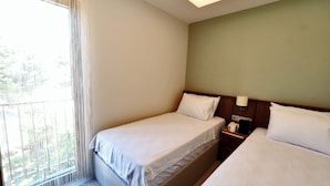 Quarto de hotel com duas camas, uma mesa de cabeceira, uma luminária e vista para o verde lá fora.