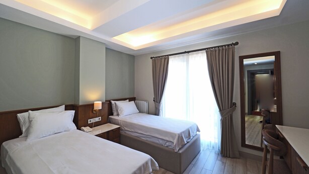 Quarto de hotel com duas camas, uma escrivaninha, uma cadeira, um espelho e uma janela com cortinas.