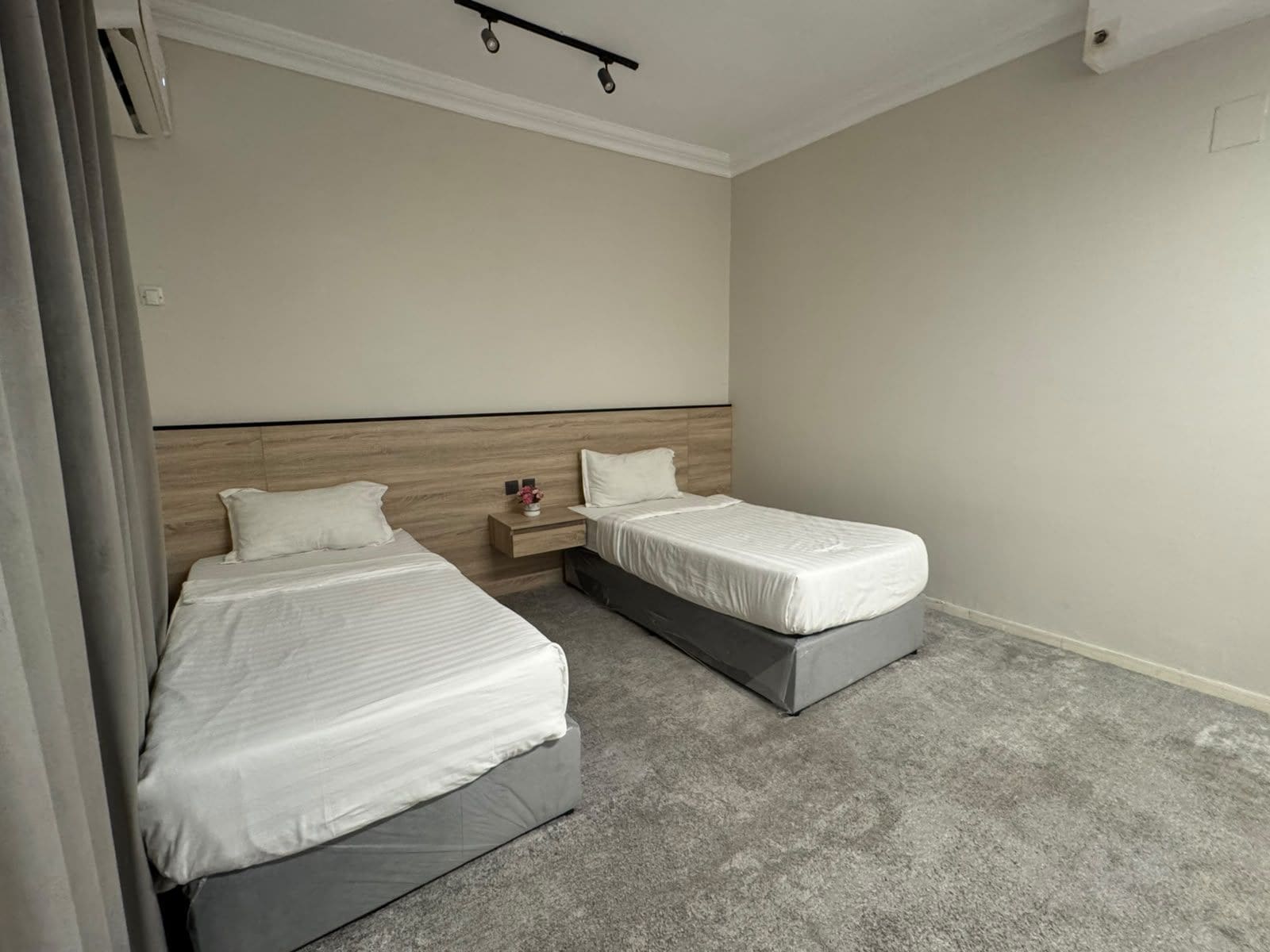 Quarto de hotel com duas camas de solteiro, cabeceira de madeira, mesa de cabeceira com um vaso e piso coberto por carpete.