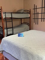 Uma cama beliche com uma etiqueta azul na parte de baixo, um edredom estampado e uma parede com decoração geométrica.