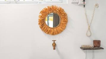 Casa de banho com lavatório de pedra, porta-toalhas, espelho com padrão de franjas, secador de cabelo e pequena prateleira com produtos de higiene pessoal.