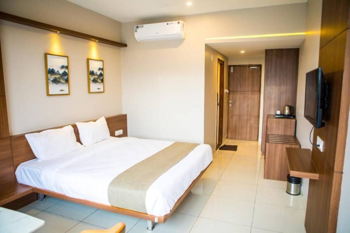 Quarto de hotel com cama, televisão, escrivaninha e uma pequena cozinha.