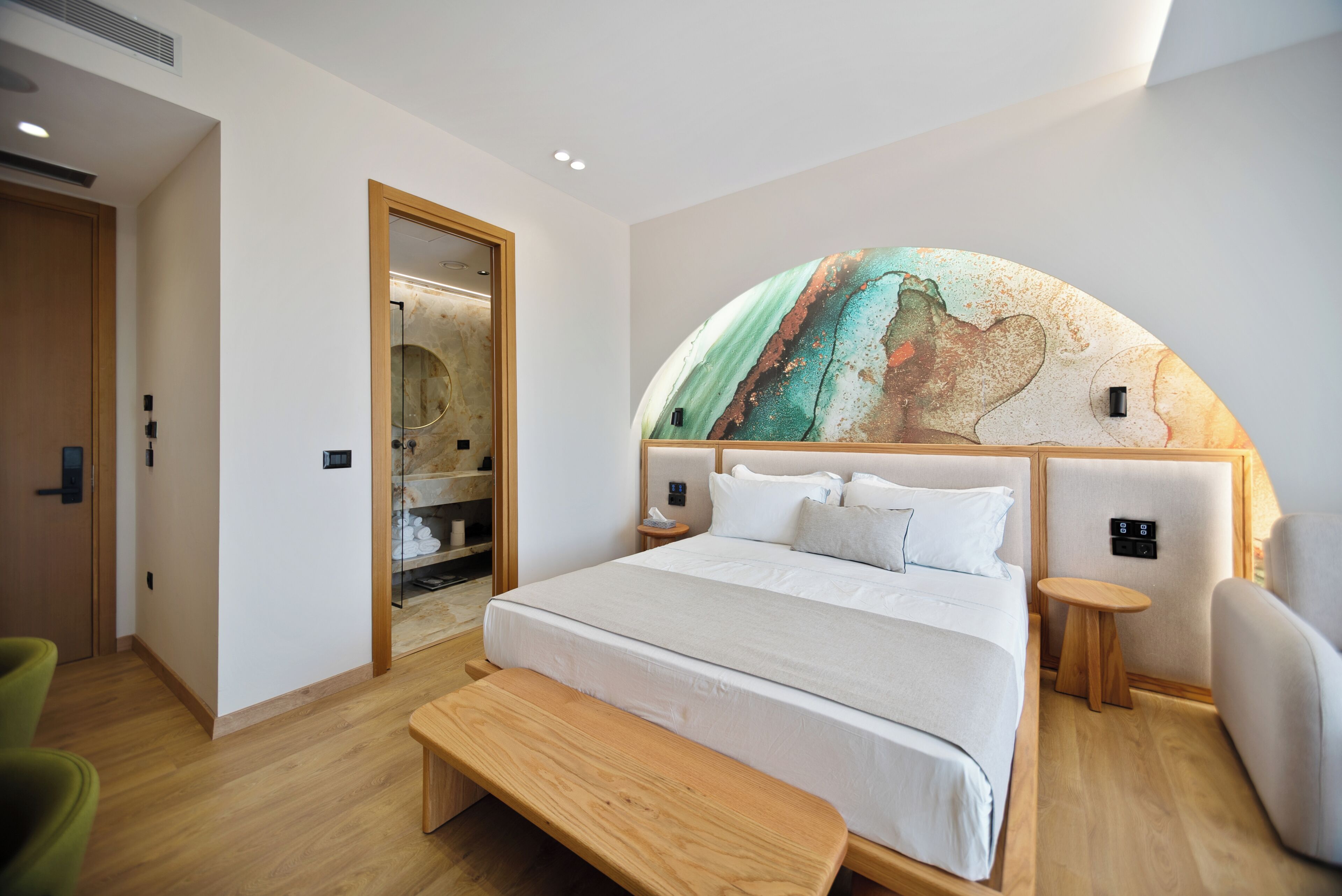 Quarto de hotel moderno com uma cama grande, um banco, um mural em curva na parede e um closet espaçoso.