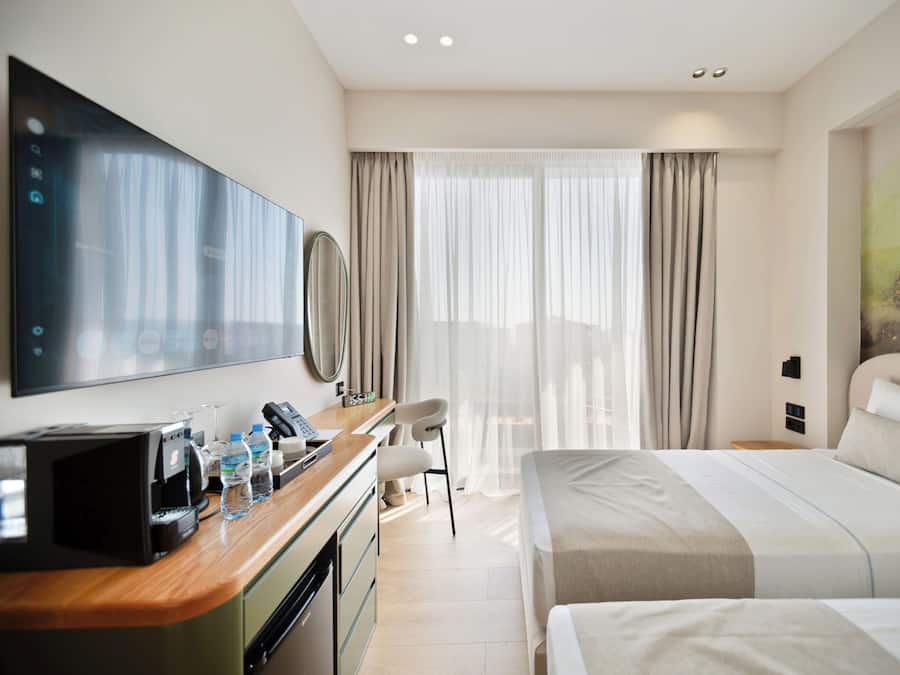 Quarto de hotel com cama, escrivaninha, telefone, televisão e janela com cortinas.