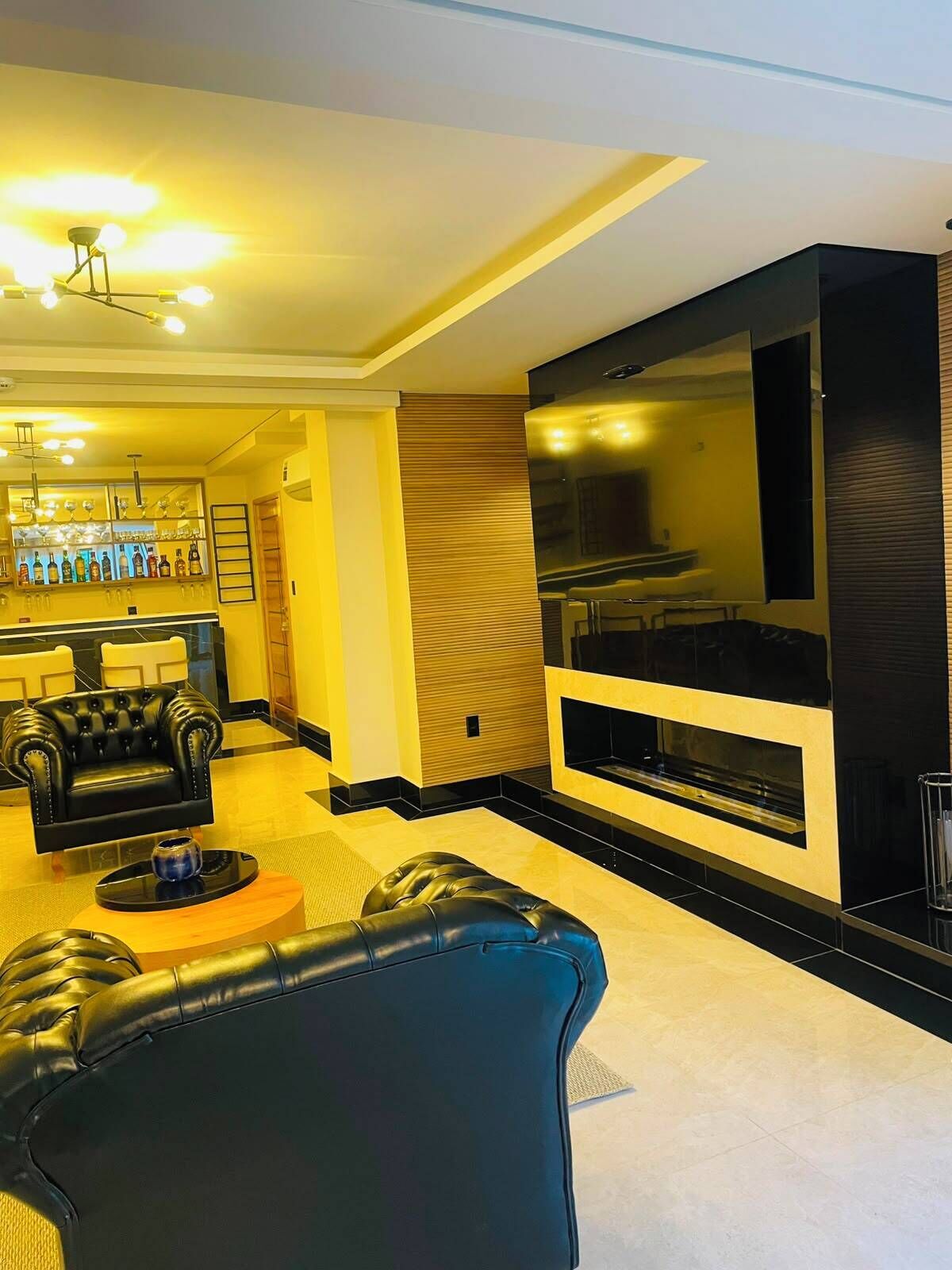 Uma sala de estar moderna com um sofá de couro preto, uma TV de tela plana e um espaço bar com garrafas.