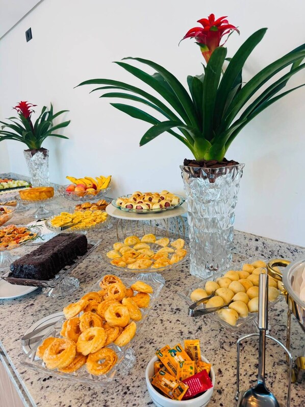 Uma mesa de buffet com diversos alimentos, incluindo doces, um bolo de chocolate e uma planta em um vaso de vidro.