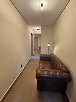 Uma sala de estar moderna com um sofá de couro, um abajur e um corredor que dá para outro quarto.