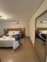 Quarto de hotel com uma cama grande, mesas de cabeceira, um aparelho de ar condicionado e um espelho.