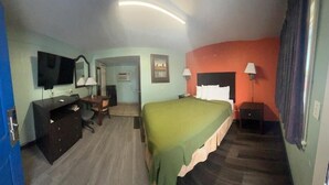 Quarto de hotel com cama, secretária, televisão e porta.