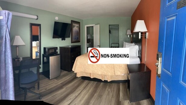 Quarto de hotel com cama, escrivaninha, cadeira, televisão e placa indicando que não é para fumantes.