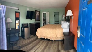 Quarto de hotel com cama, escrivaninha, cadeira, televisão e uma porta azul.