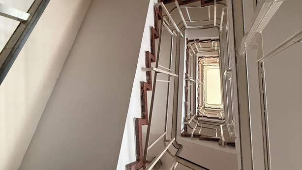 Uma escadaria em espiral com corrimão de metal, que leva a um andar superior.