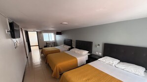 Quarto de hotel com três camas, uma mesa e uma televisão.