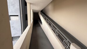 Um corredor estreito com guarda-corrimão de metal, chão de concreto e parede bege.