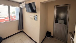 Quarto com televisão na parede, janela com cortinas, porta com janela e lixeira.