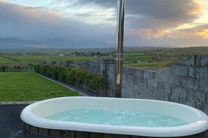 Uma banheira de hidromassagem com vista para uma paisagem rural e montanhas ao fundo.
