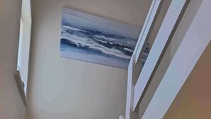 Uma escadaria com degraus carpetados, corrimãos brancos e um quadro de uma paisagem marítima na parede.