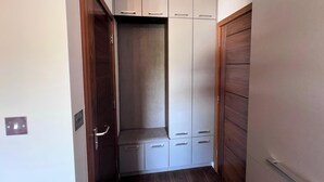 Um corredor estreito com uma porta de madeira à esquerda e um guarda-roupa com vários compartimentos à direita.