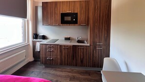 Cozinha compacta com armários de madeira, micro-ondas, pia e torradeira.
