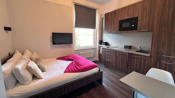 Quarto compacto com uma cama, um pequeno espaço de cozinha e uma televisão.