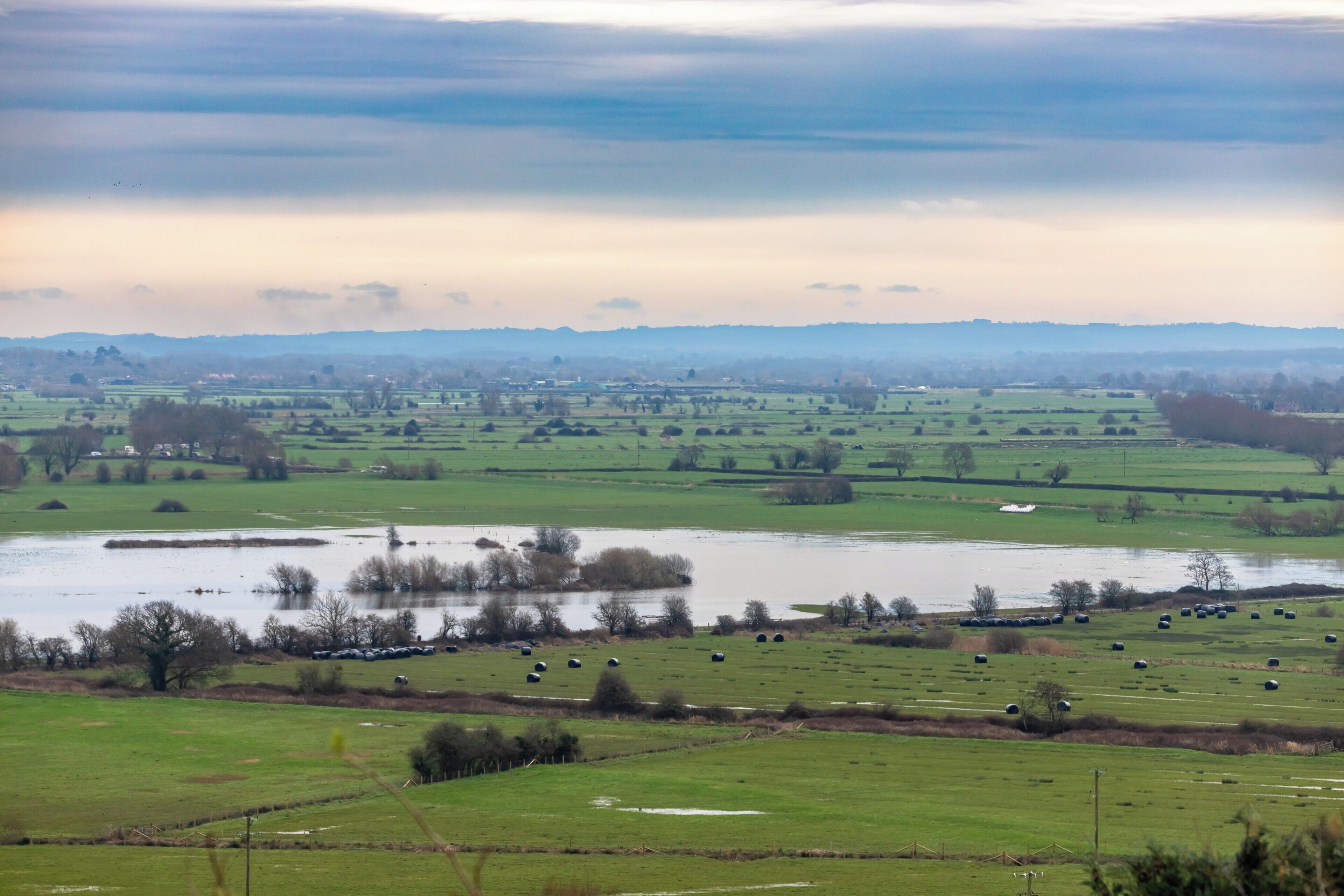 Paisagem rural com campos, um rio e colinas ao longe.