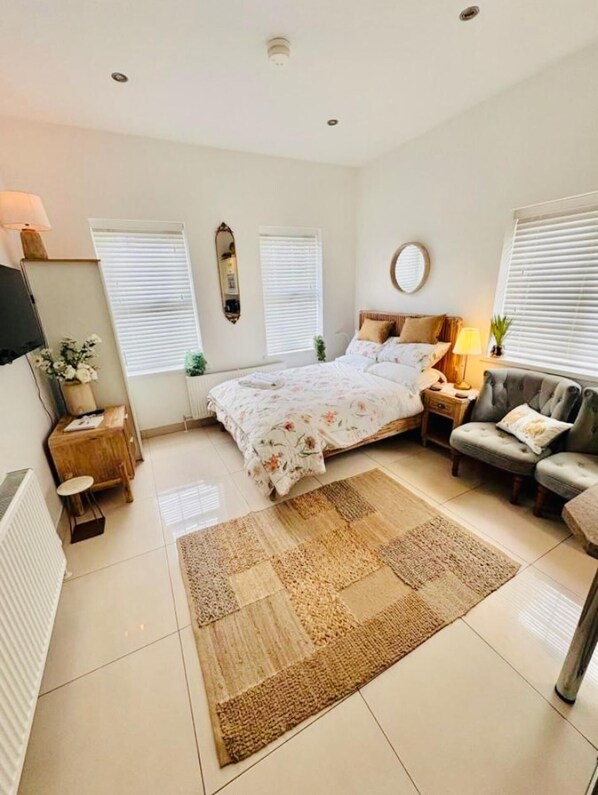 Quarto com cama, mesas de cabeceira, sofá, tapete e televisão.