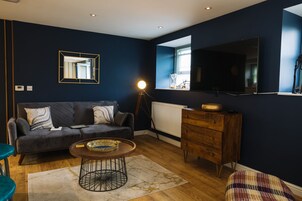 Quarto com parede azul escura, um sofá, uma mesa de centro, cômoda e televisão.