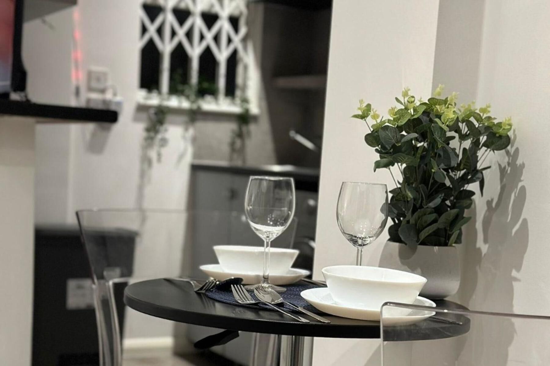 Uma mesa de jantar com um vaso de planta, duas taças de vinho e talheres.