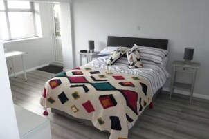 Quarto com cama, mesas de cabeceira, janela e porta.